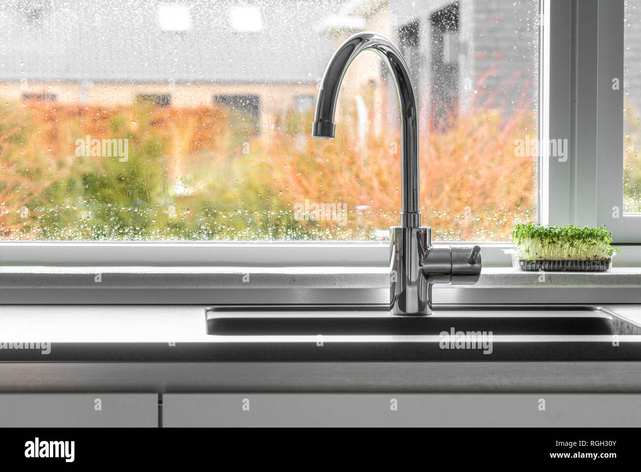 Chrome faucet by a kitchen sink with a wet window in the background ...
