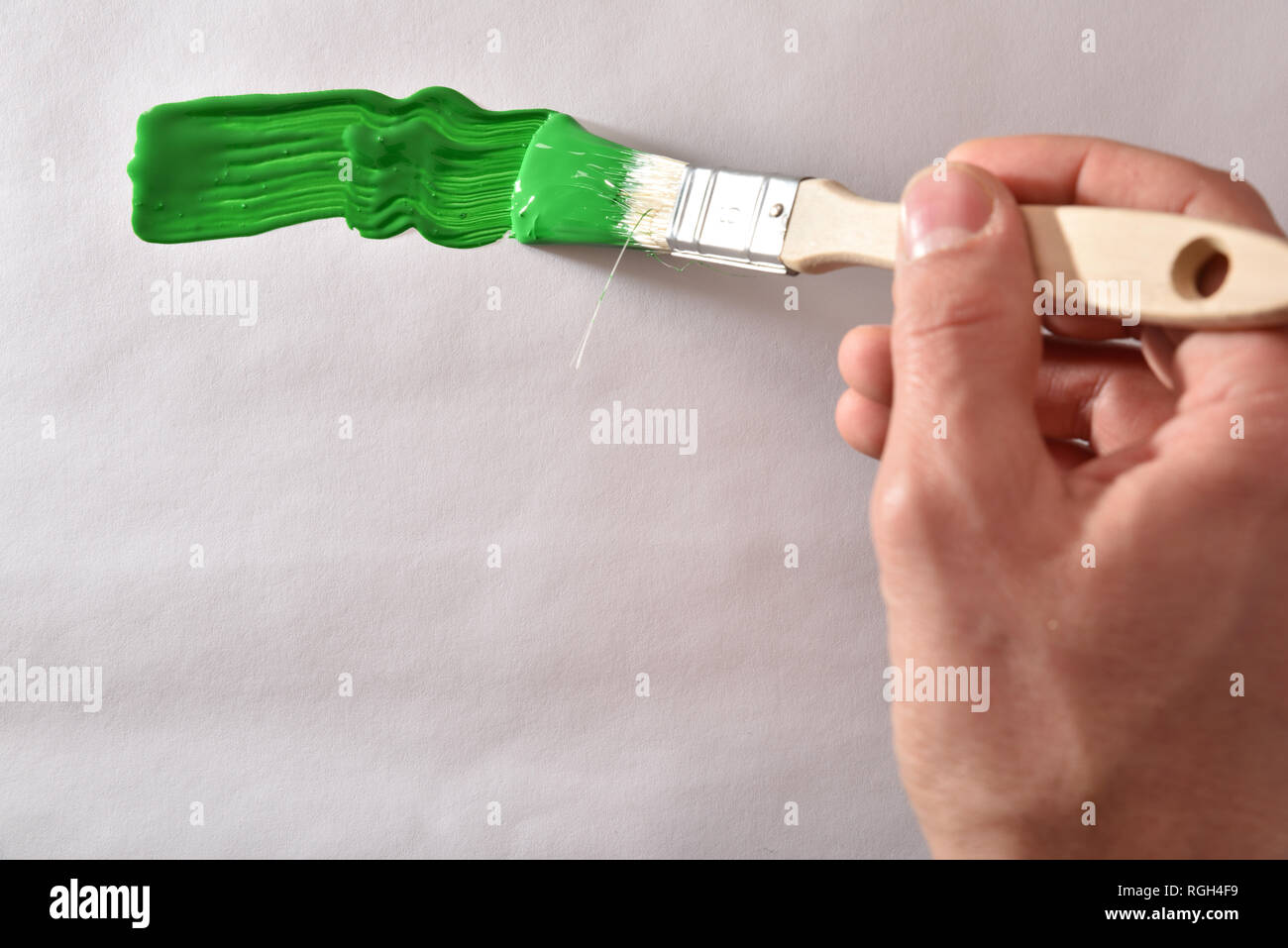 Hand painting with paintbrush and green paint on white textured ...