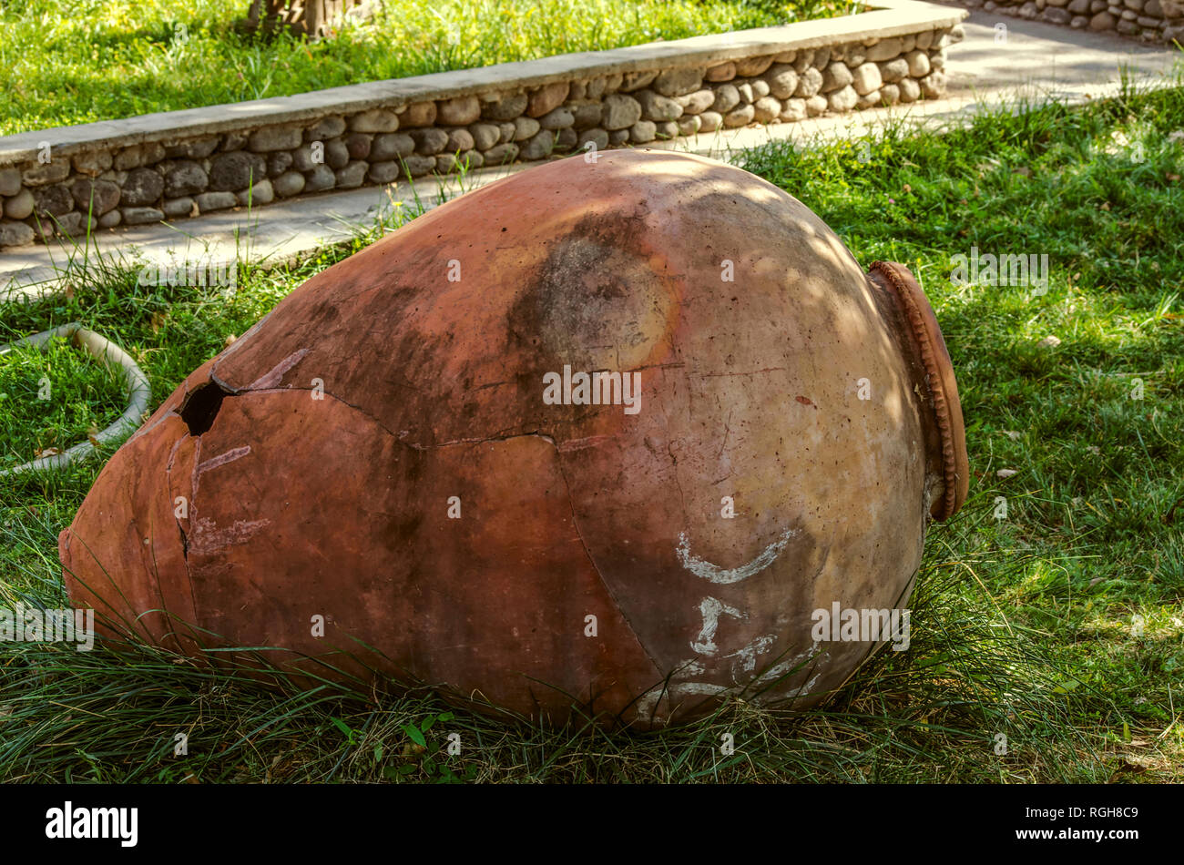 An old large cracked pitcher of red clay is lying on the green grass in ...