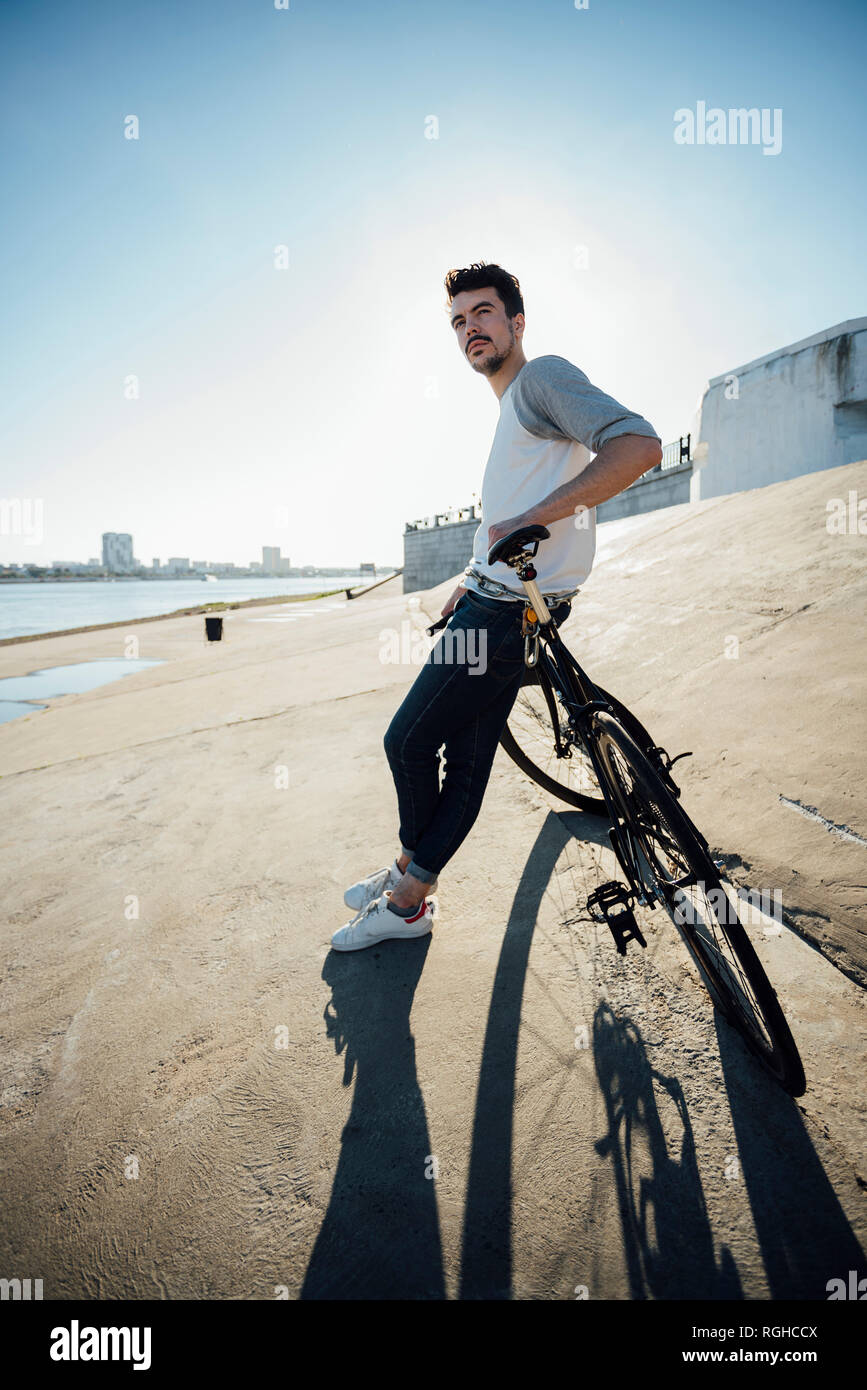Young man with commuter fixie bike having a break at concrete wall ...
