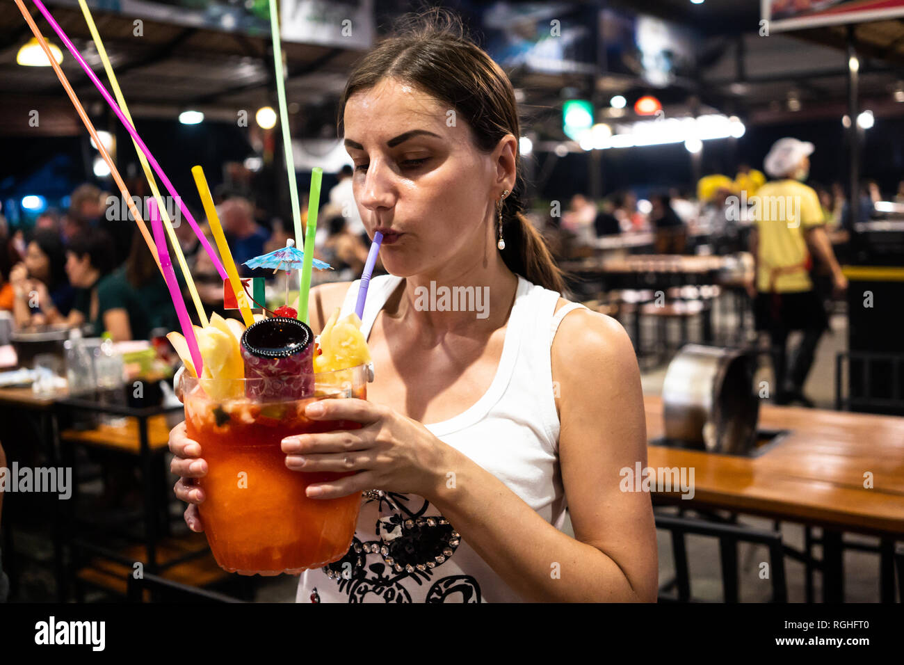 The girl drinks a big cocktail from a straw in a nightclub, a night ...