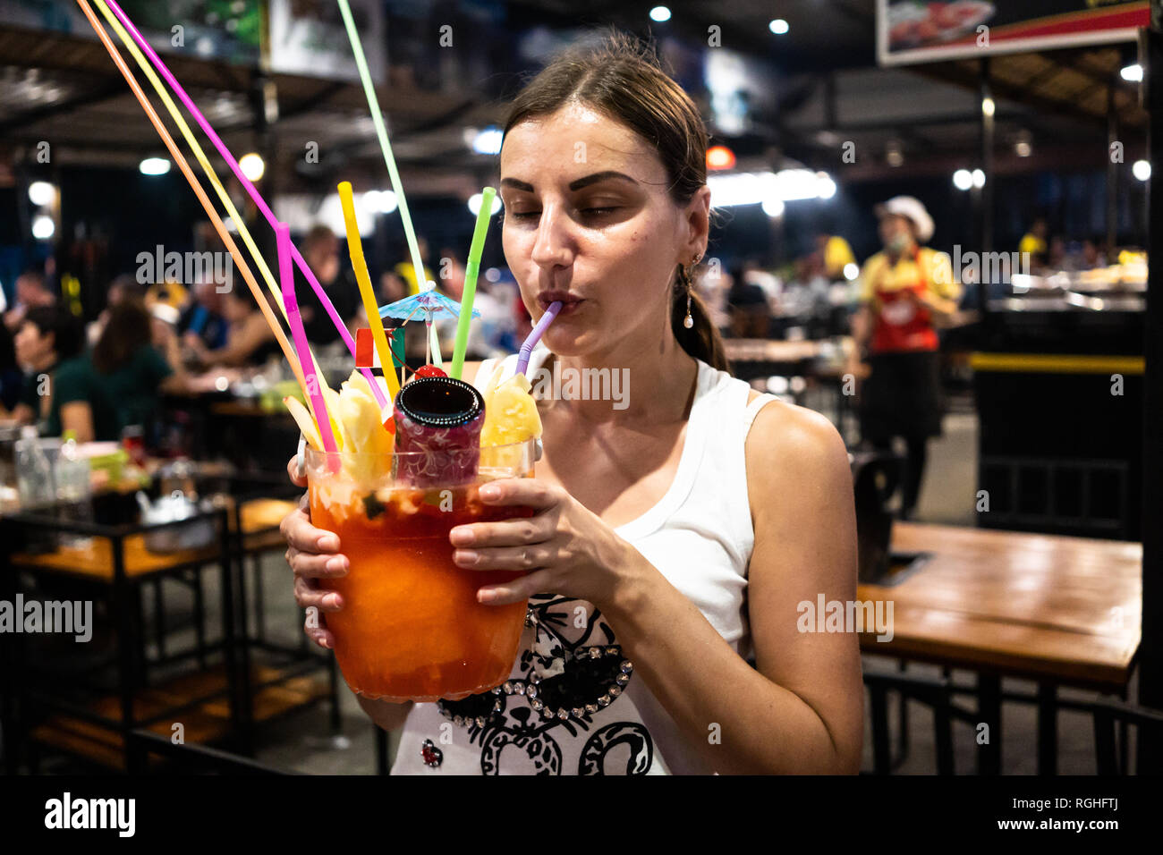 The girl drinks a big cocktail from a straw in a nightclub, a night ...