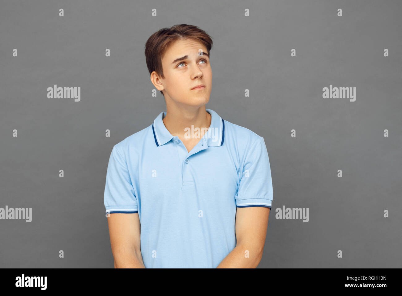 Young man standing isolated on grey wall looking up with hope Stock ...