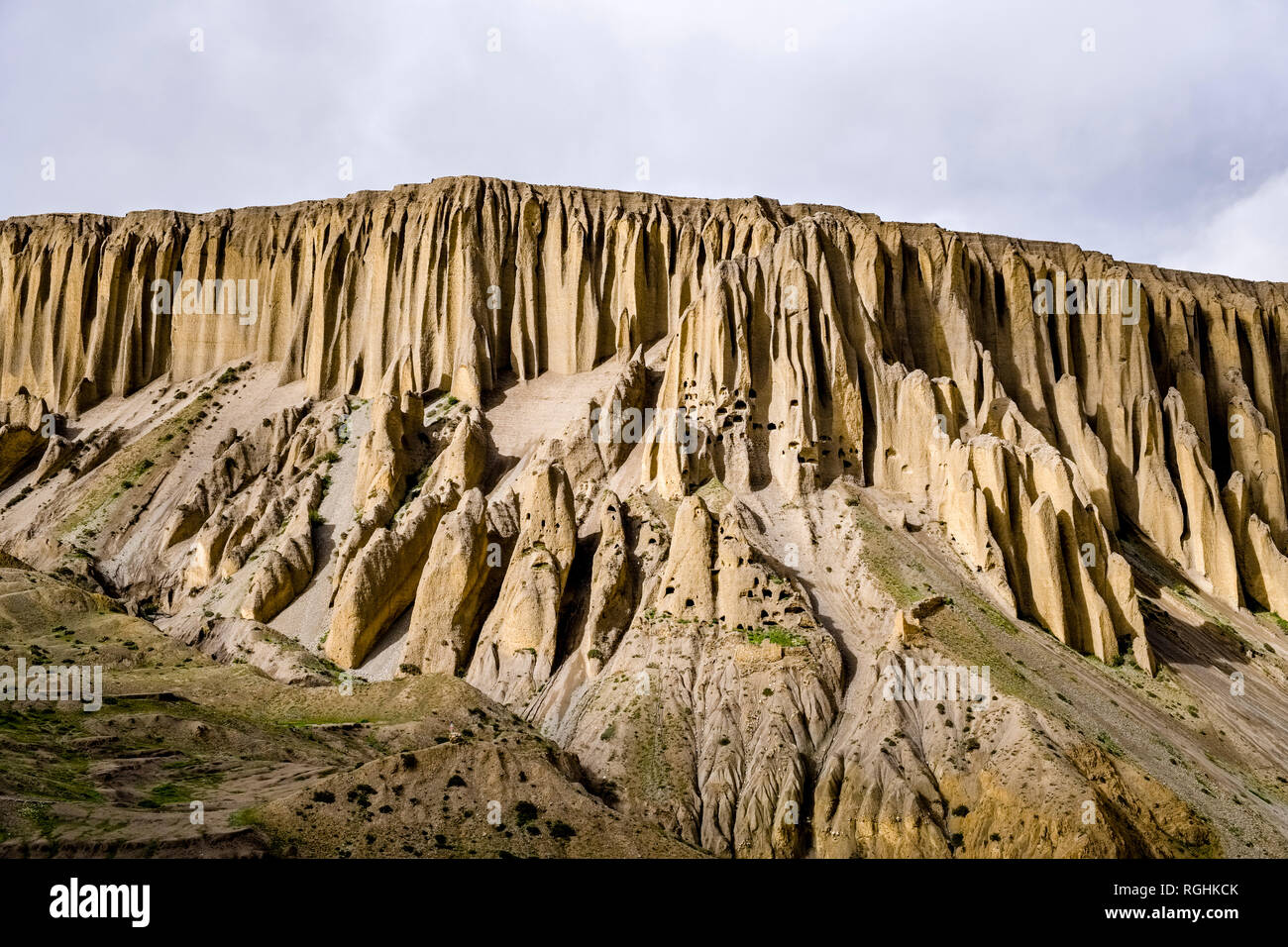 Vertically formed rock cliff with man made caves, dark monsoon clouds ...