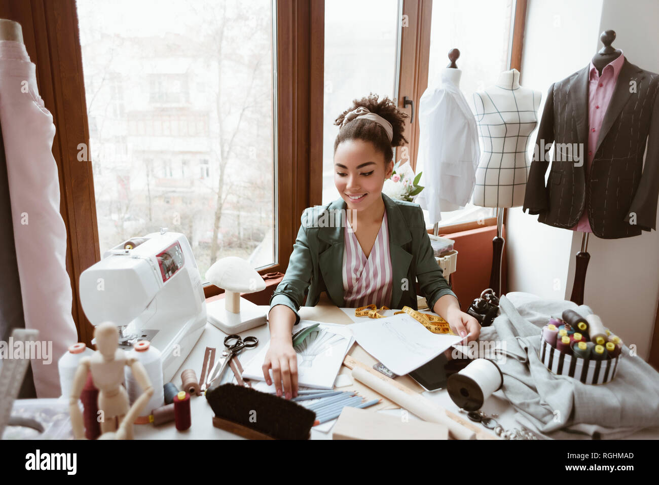 Modeling new design. Young woman tailor with sewing machine is modeling ...