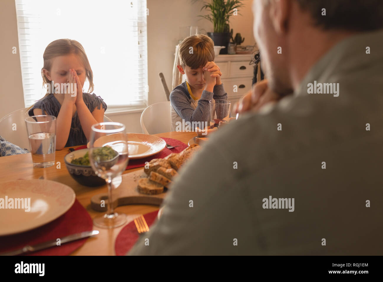 Over shoulder view of family praying before having food on dining table ...