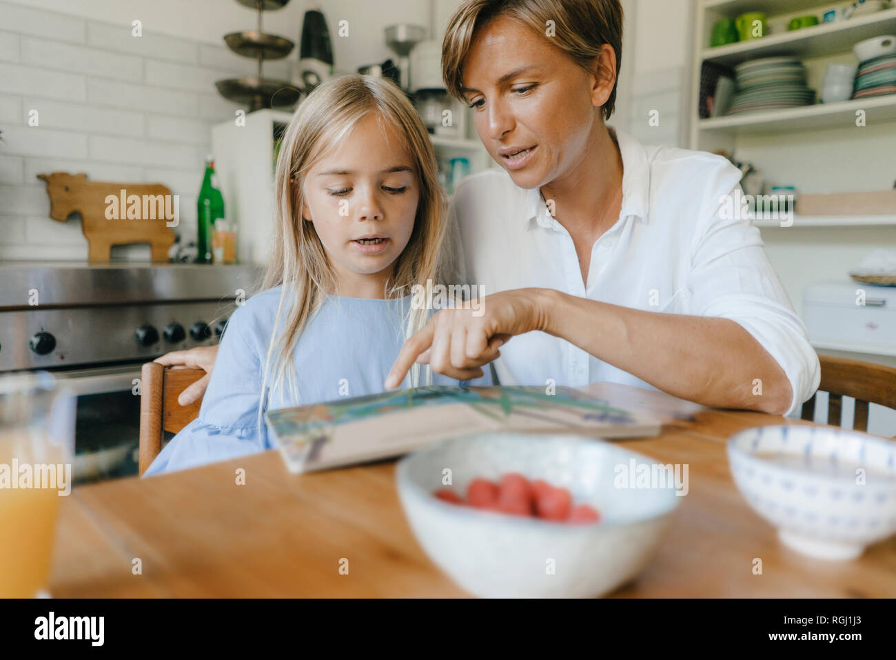 Mother and daughter reading book at table at home together Stock Photo ...