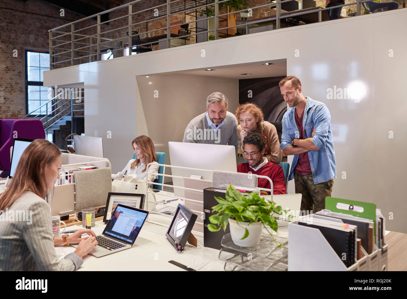 Colleagues looking over shoulder of young man working in modern office ...