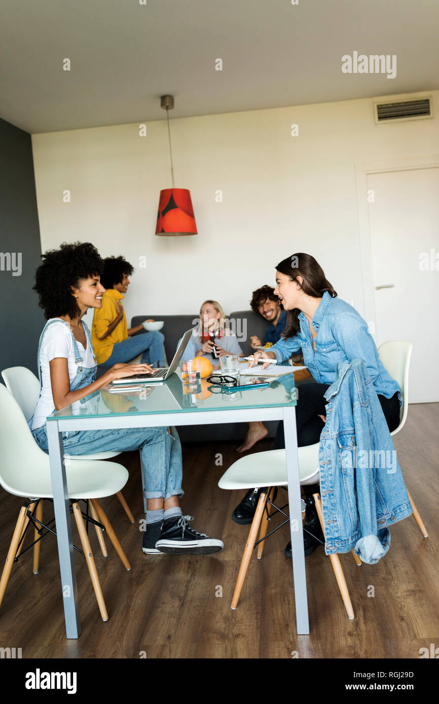 Women using laptop and notebook at dining table with friends in ...