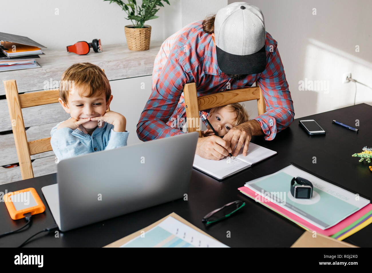 Father writing in notebook while children are playing at his desk Stock ...
