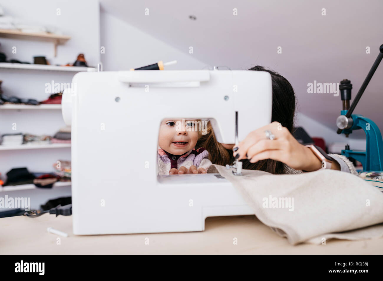 Little daughter watching her mother using sewing machine at home Stock ...
