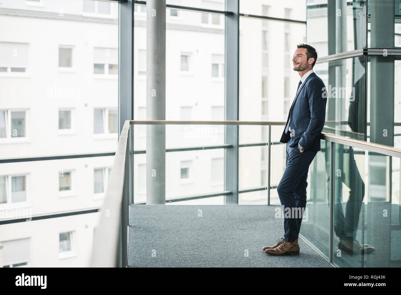 Successful businessman standing in office building, looking out of ...