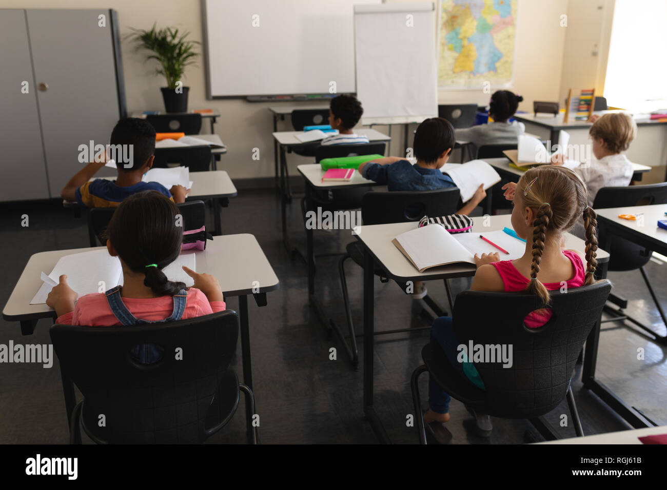 Rear view of focused kids studying in classroom sitting at desks in ...