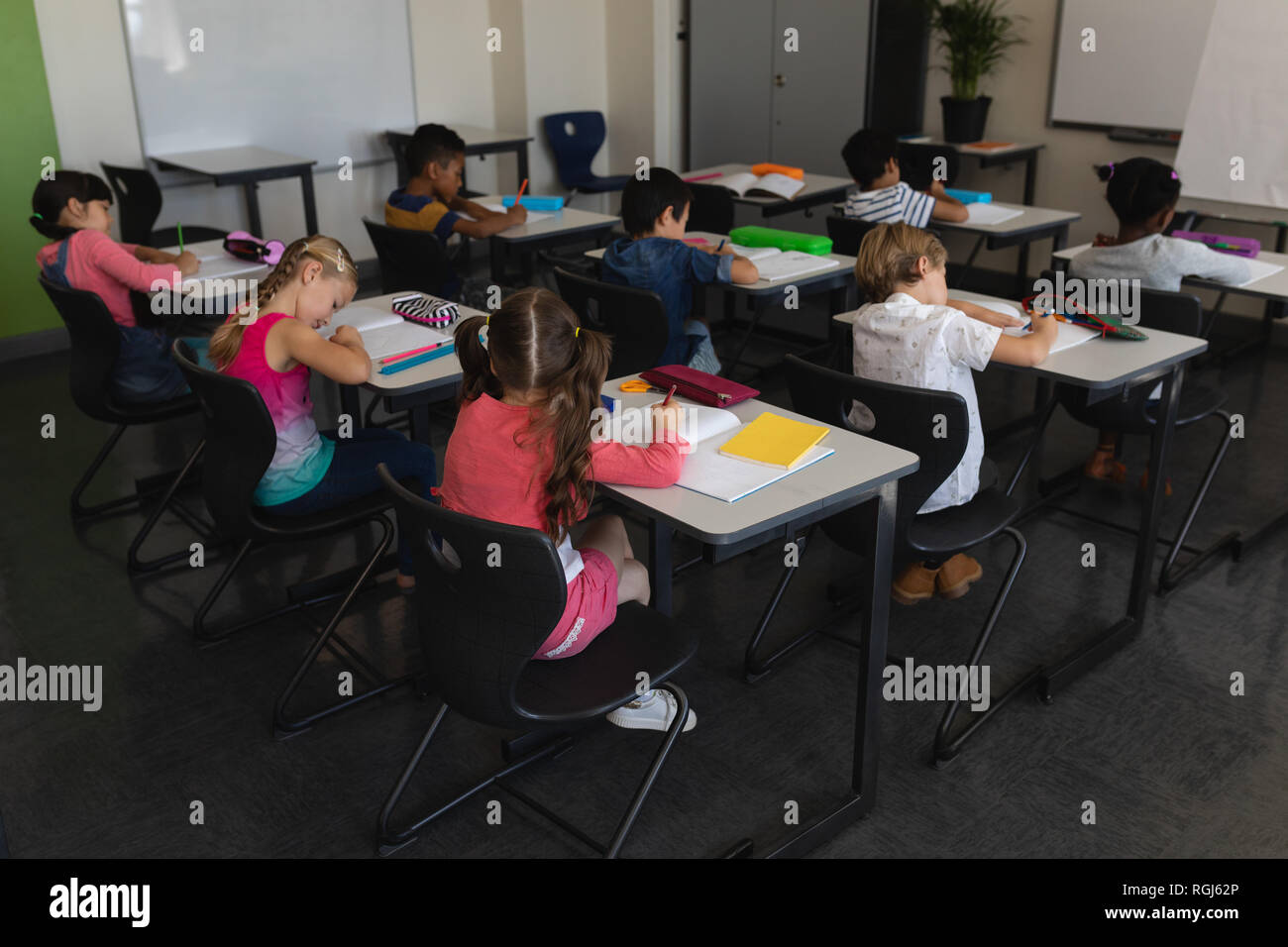 Rear view of kids studying and sitting at desk in classroom in school ...