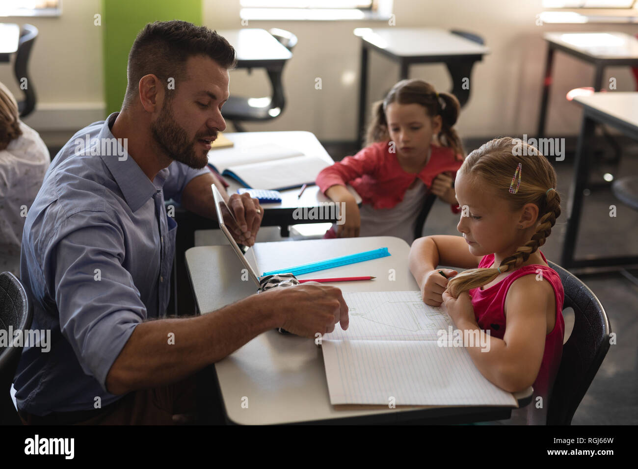 Side view of young school teacher helping girl with study while ...