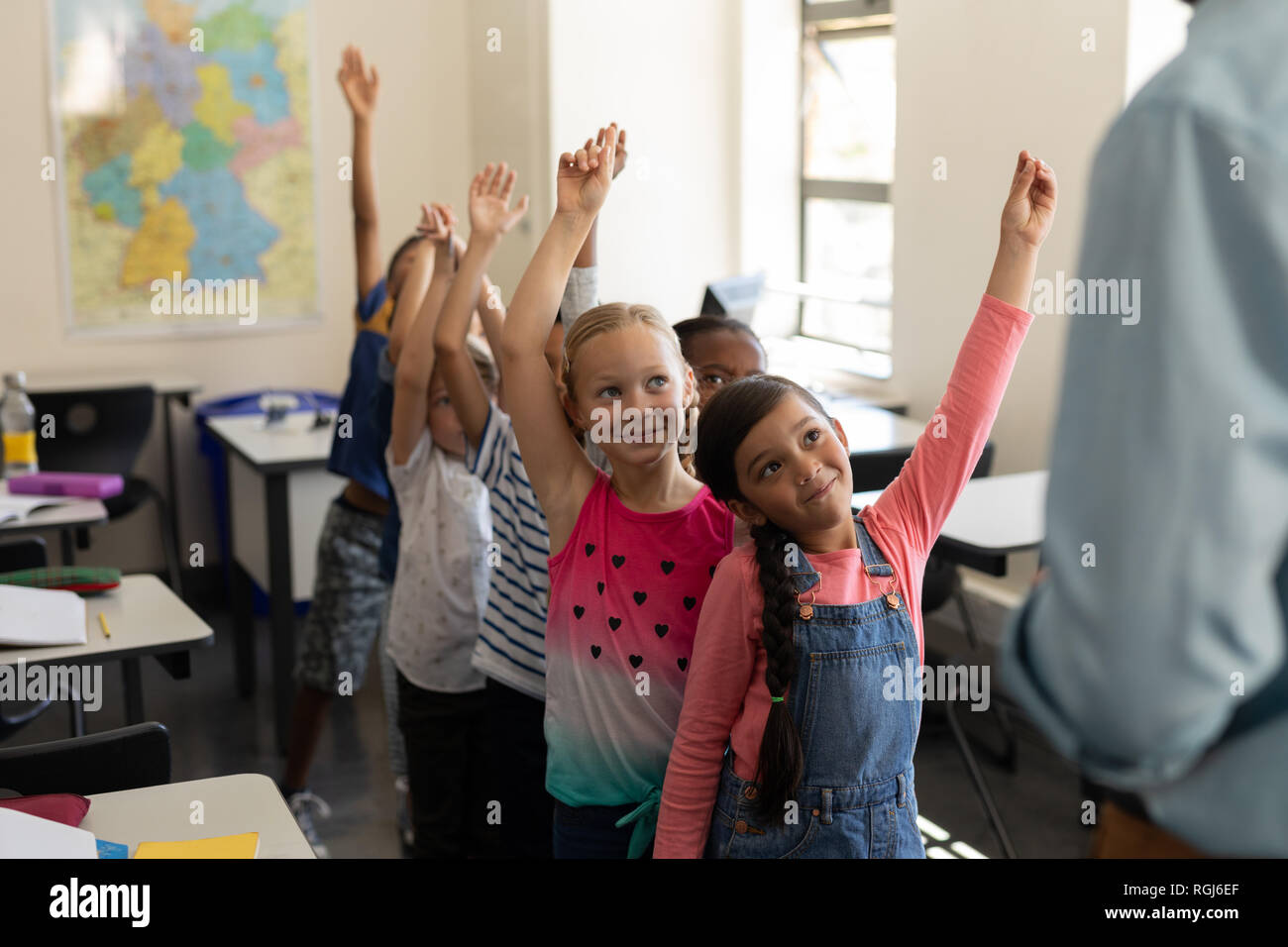 School kids standing in row and raising hand in classroom of elementary ...