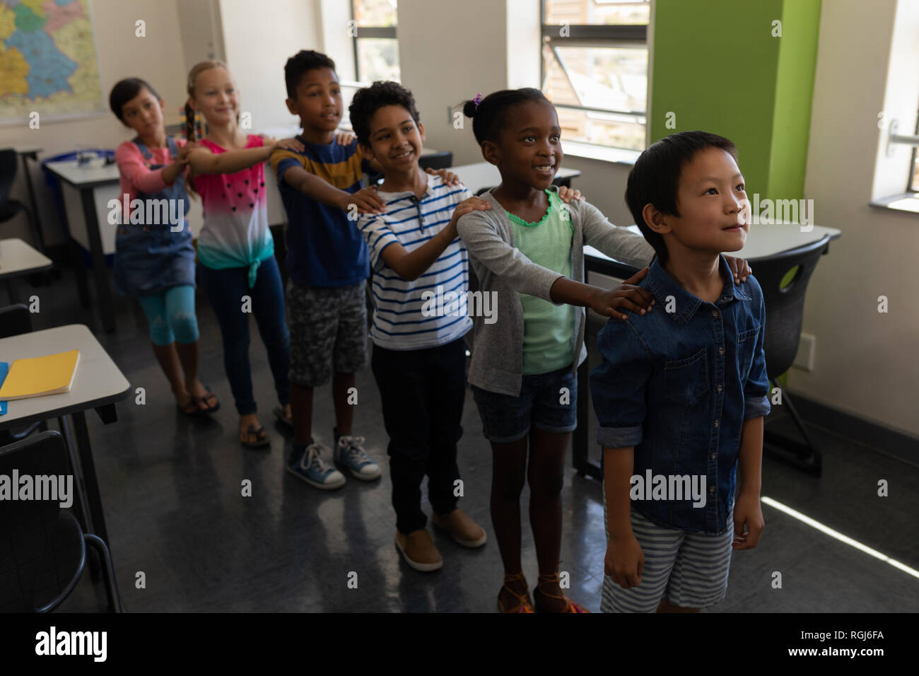 Side view of school kids standing in row with their hands on shoulder ...