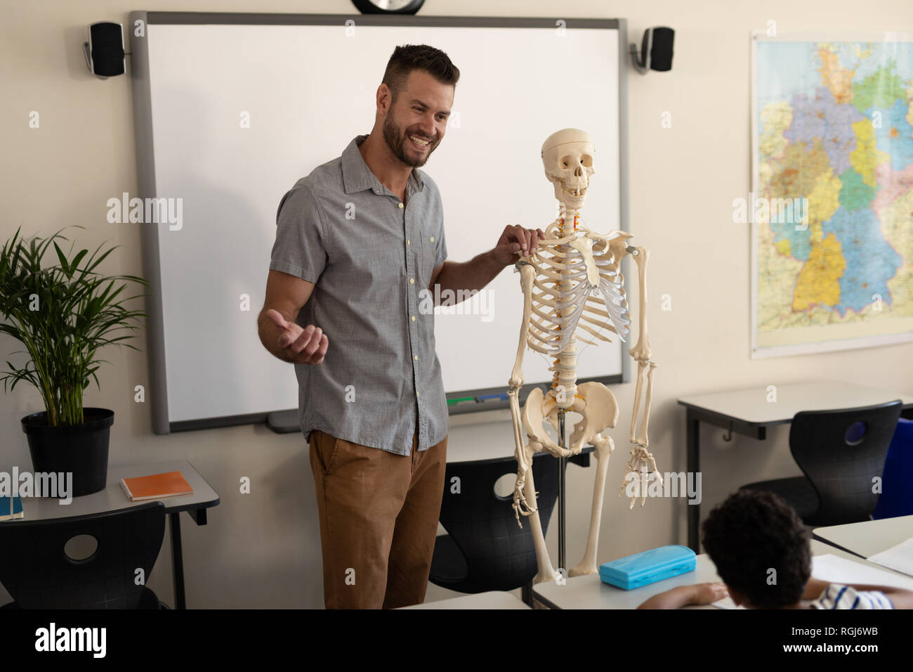 Side view of happy male teacher explaining human skeleton model in ...