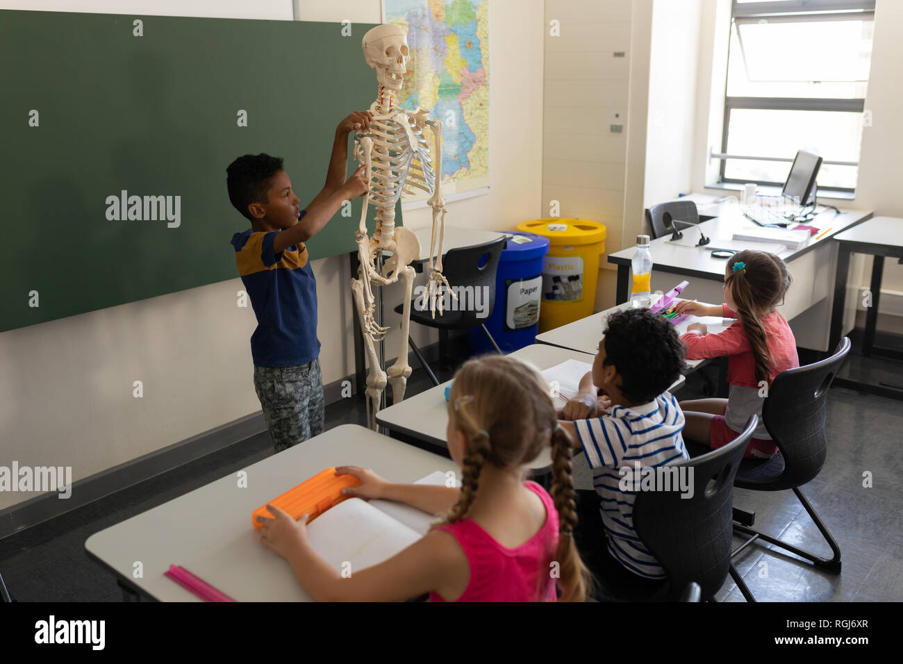 Side view of schoolboy explaining human skeleton model in classroom ...
