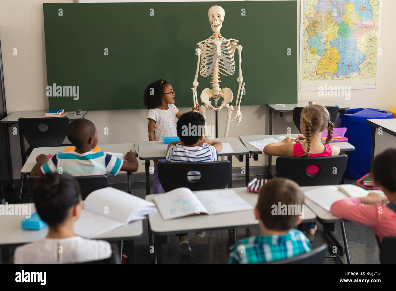 Rear view of little schoolgirl explaining human skeleton model in ...