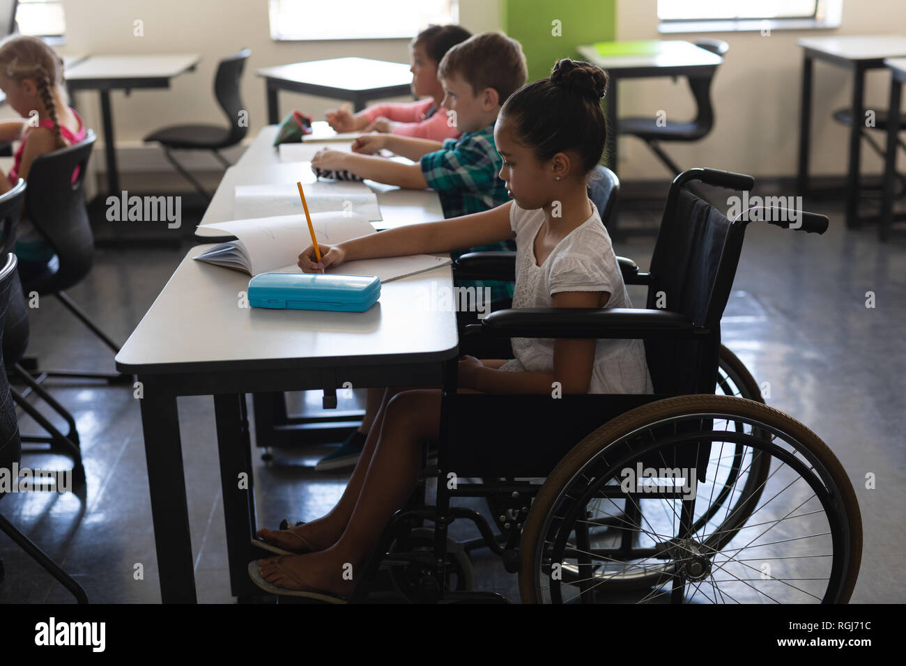 Side view of disabled schoolgirl with classmates studying and sitting ...