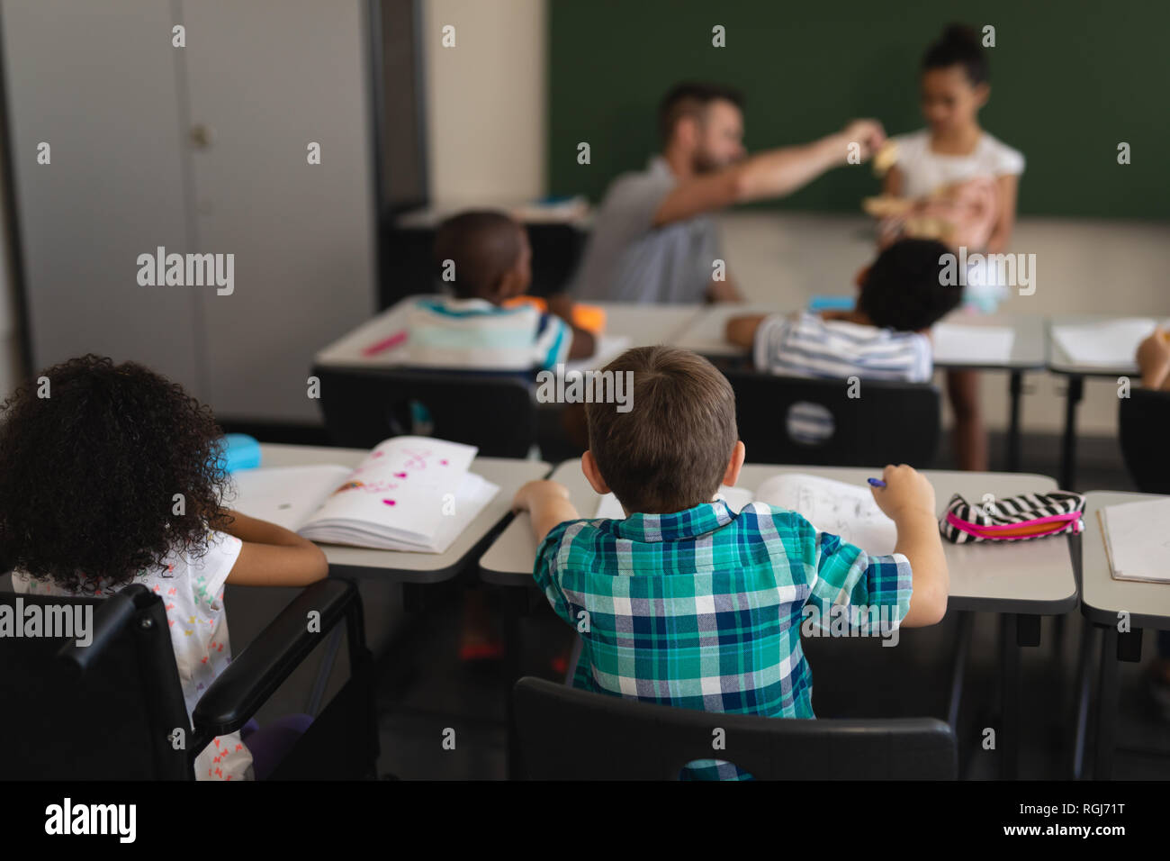 Rear view of schoolkids studying and sitting at desk in classroom of ...