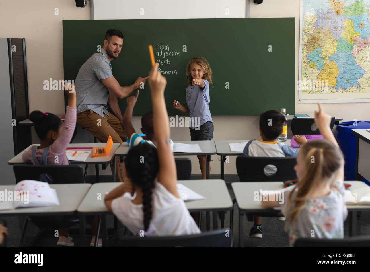 Rear view of schoolboy pointing finger towards classmates in classroom ...
