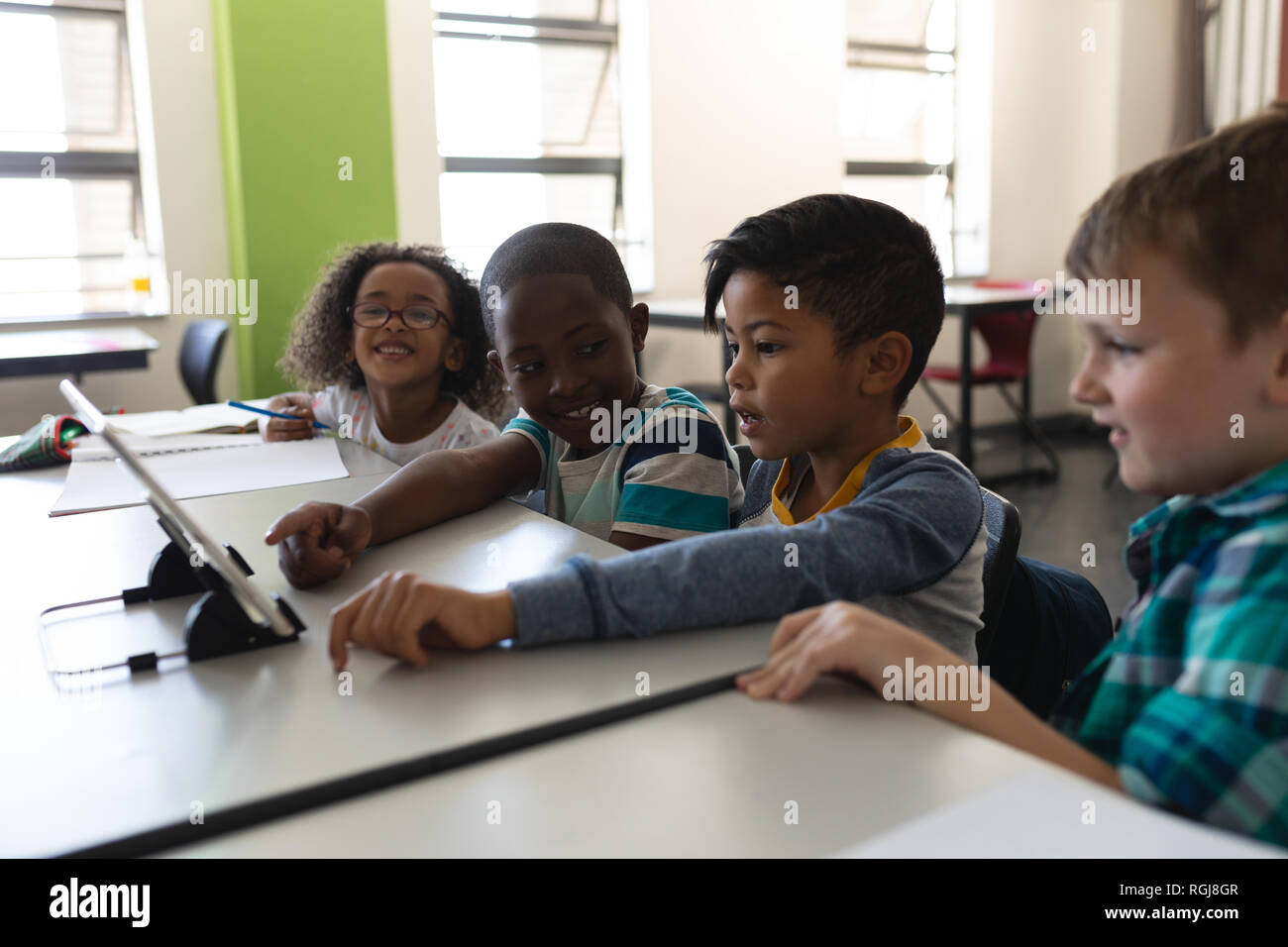 Side view of curious schoolkids studying on digital tablet while ...