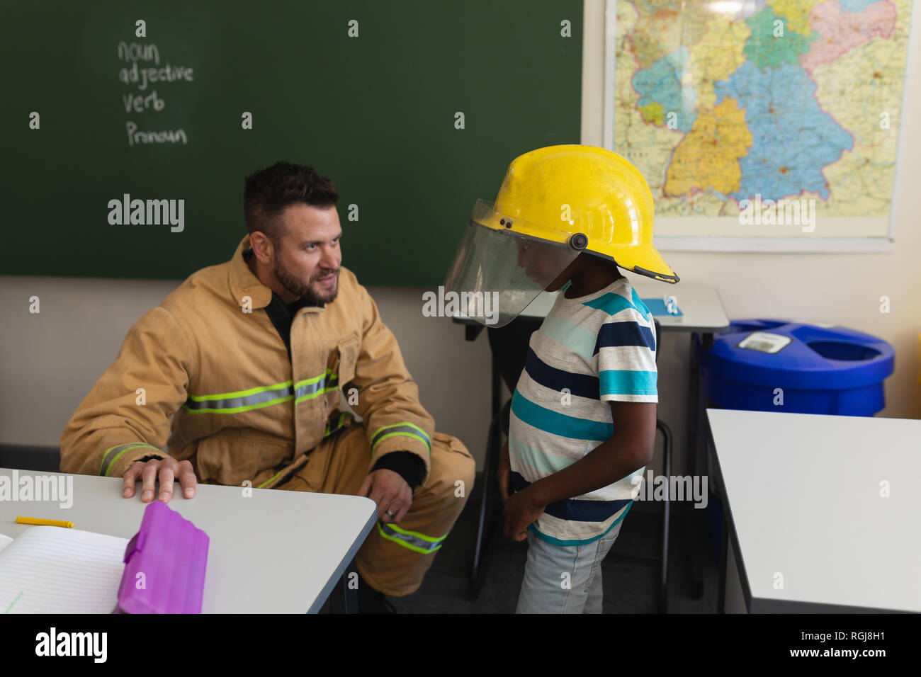 Male firefighter teaching schoolboy about fire safety in classroom of ...