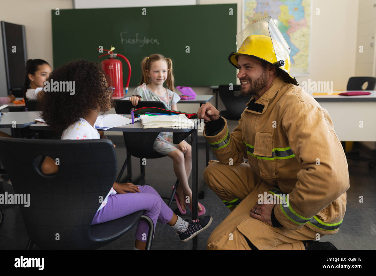 Side view of male firefighter teaching schoolkids about fire safety in ...
