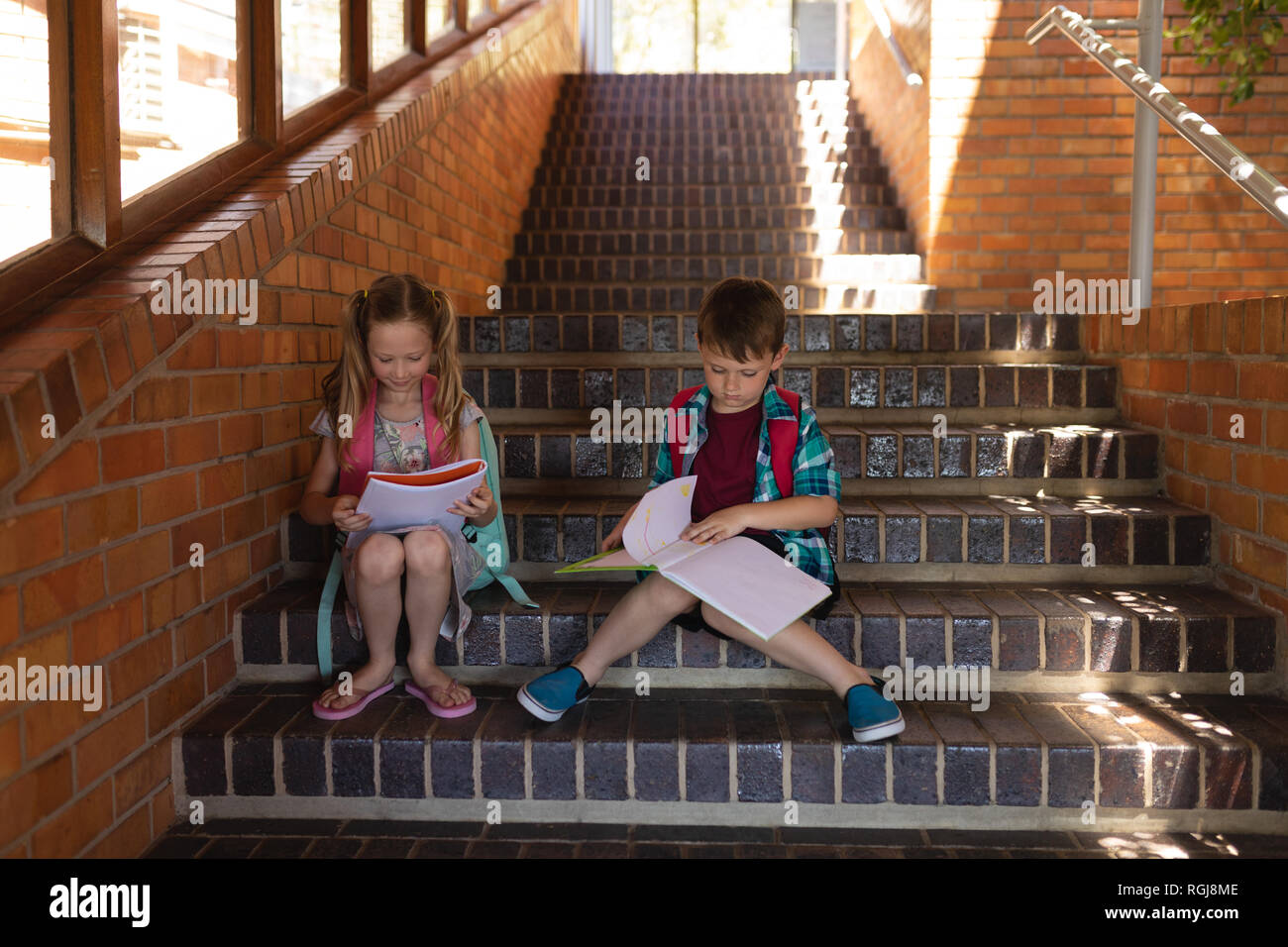 Schoolkids reading book while sitting on stairs of elementary school ...