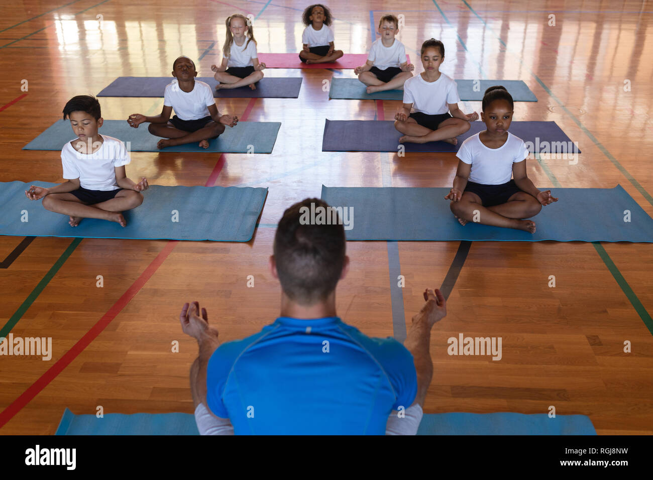 High angle view of yoga teacher teaching yoga to school kids in school ...
