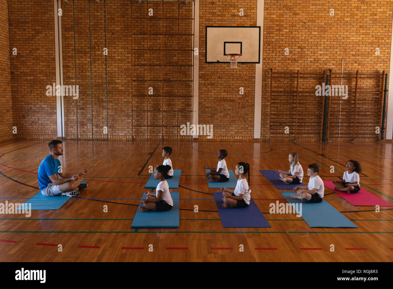 Side view of yoga teacher teaching yoga to school kids in school ...