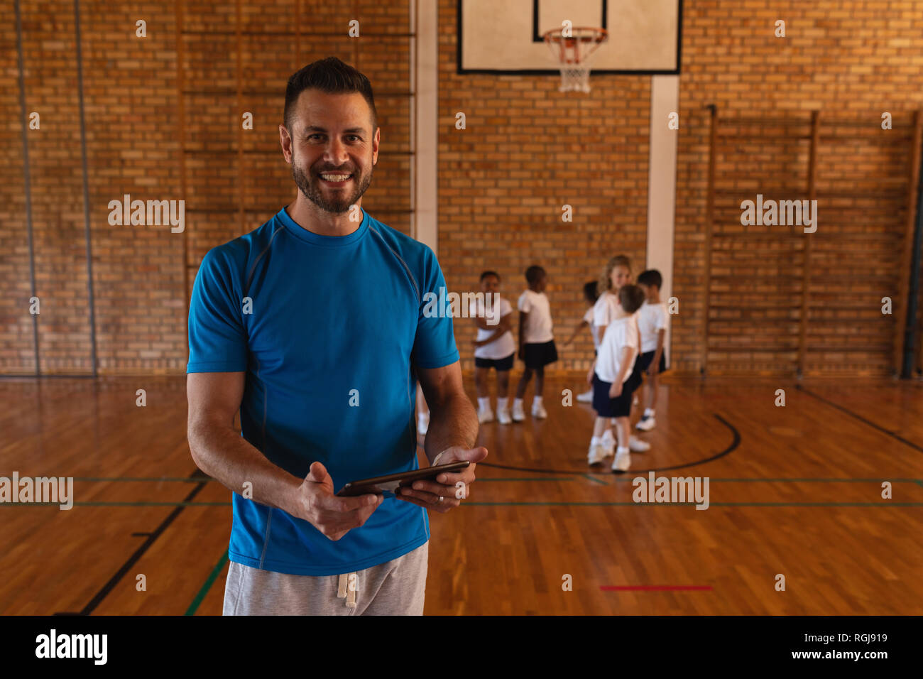 Front view of happy basketball coach using digital tablet at basketball ...