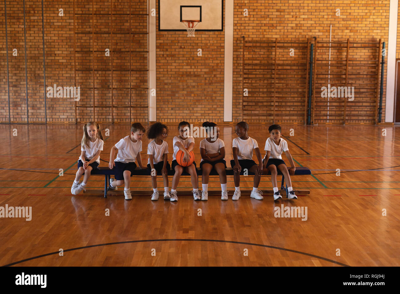 Front view of schoolkids with basketball sitting on bench at basketball ...