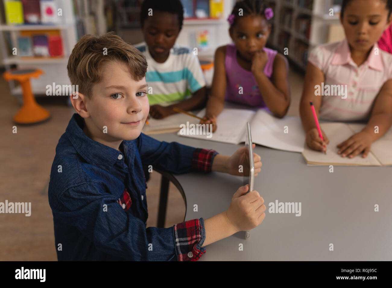 Side view of smiling schoolboy holding digital tablet and looking at ...