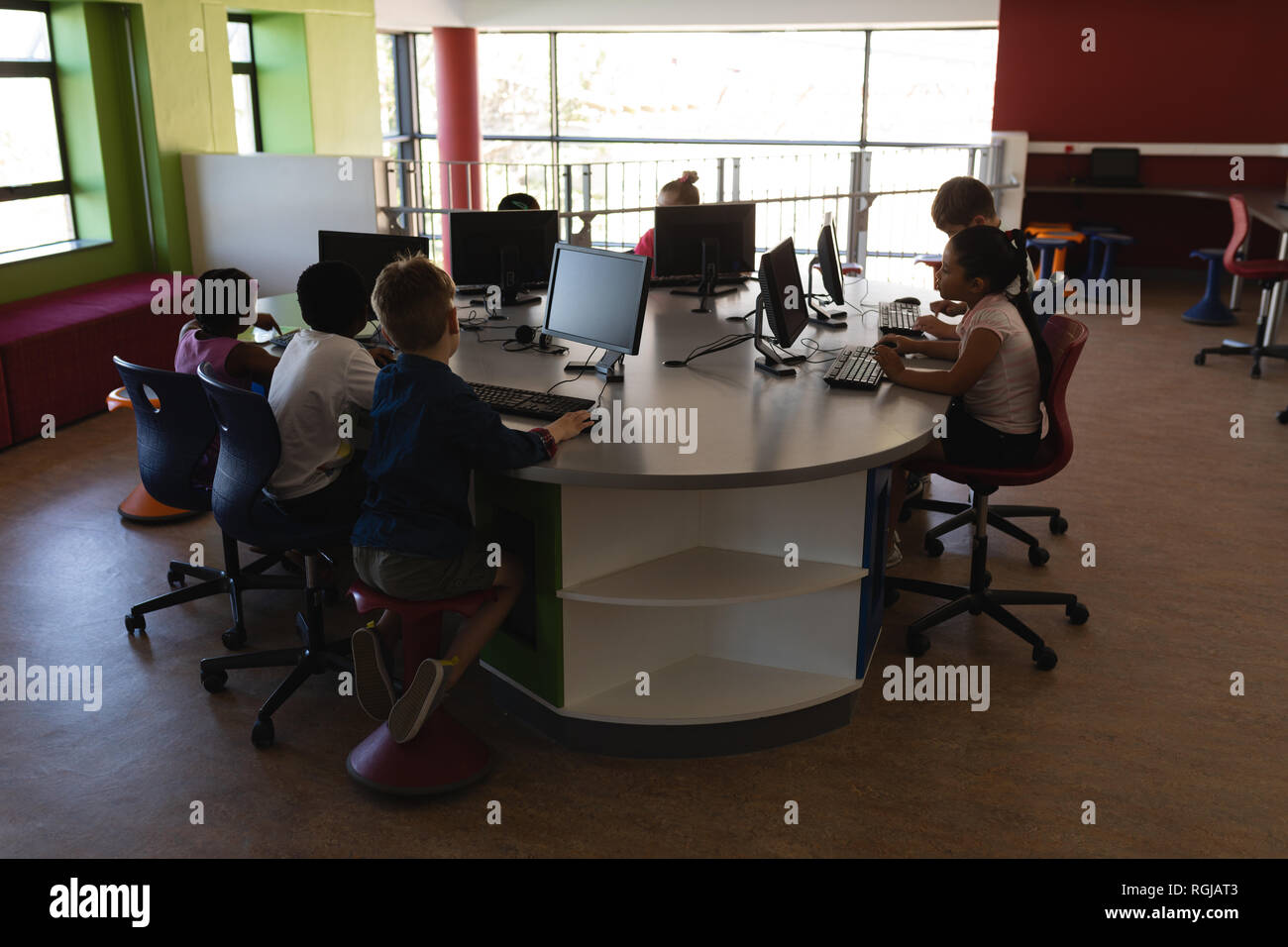 Rear view of a group of schoolkids studying on desktop pc in school ...