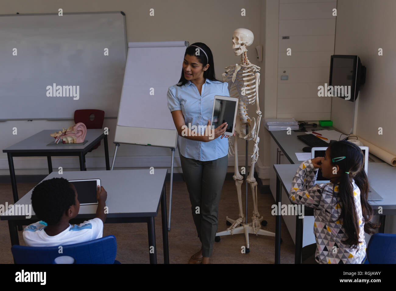 Front view female teacher teaching schoolboy on digital tablet at table ...