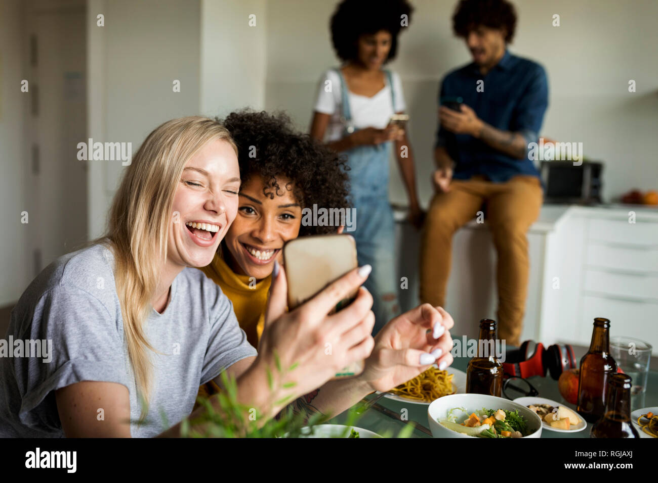 Happy girlfriends with cell phone sitting at dining table Stock Photo ...