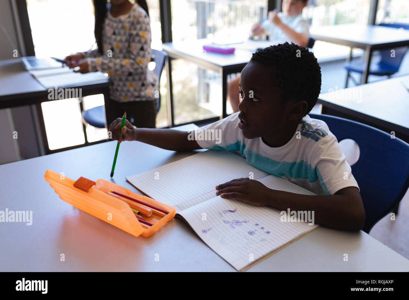 Side view of schoolboy sitting at desk and looking away in classroom of ...