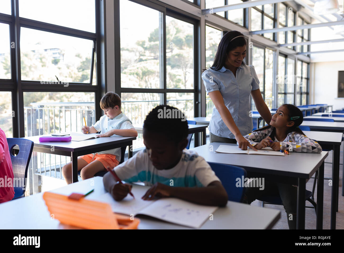 Side view young female teacher teaching schoolkid at desk in classroom ... Side view young female teacher teaching schoolkid at desk in classroom ...