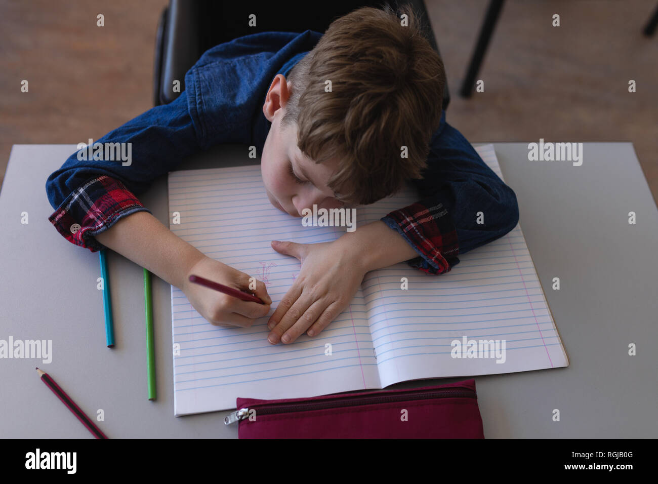 Schoolboy writing on notebook and sitting at desk in classroom Stock ...