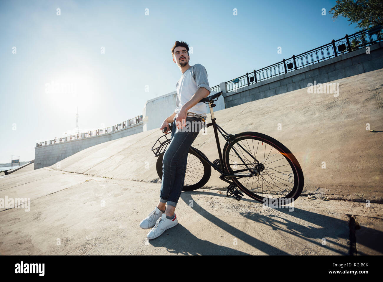 Young man with commuter fixie bike having a break at concrete wall ...