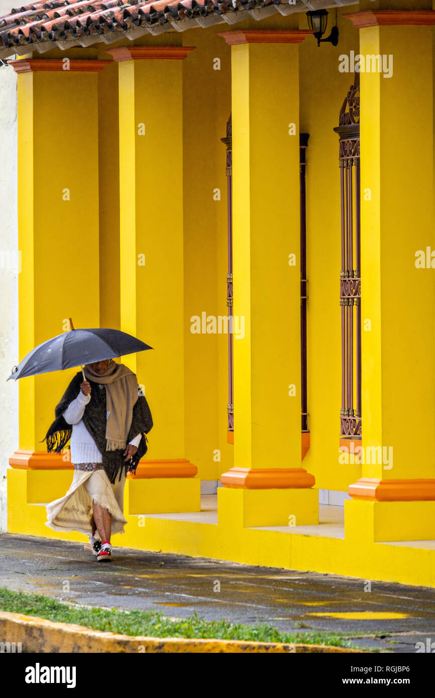 A woman with an umbrella walks past a colorful colonnade style building ...