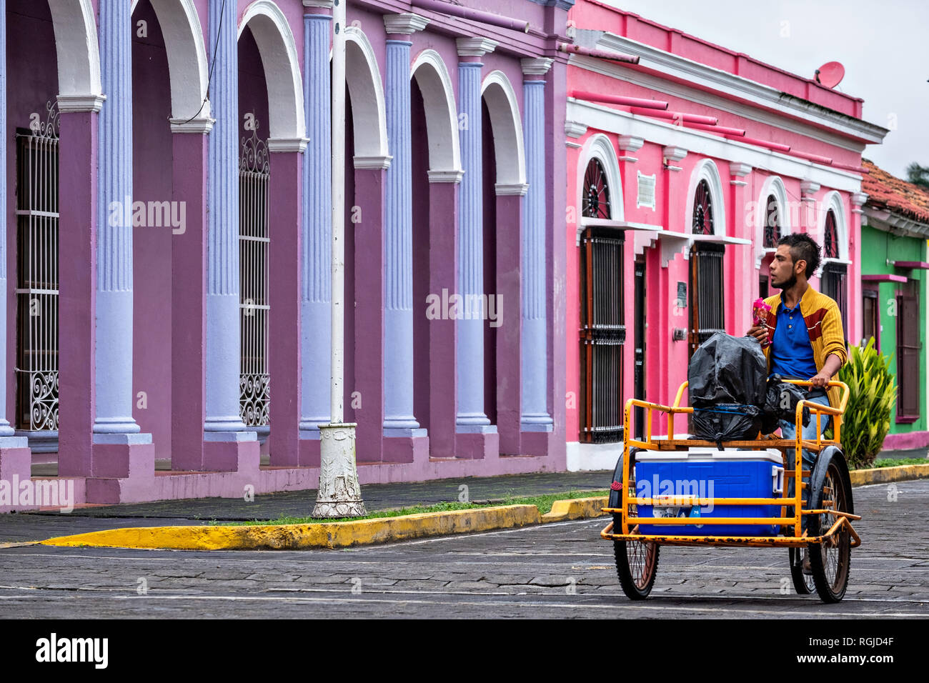 A vendor rides his cargo cycle past colorful colonnade style buildings ...
