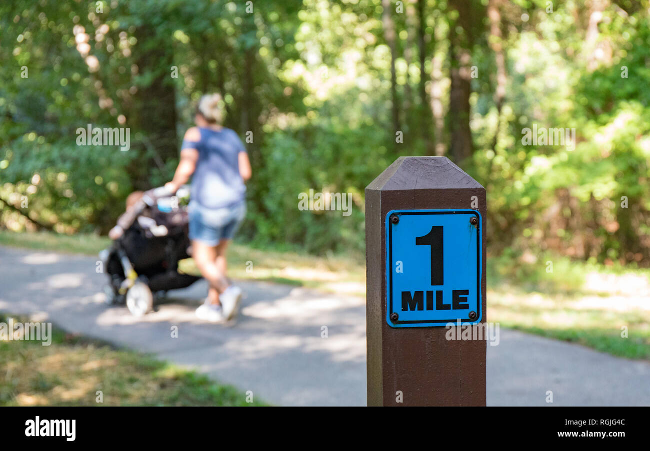 A one mile marker sign post beside a paved pathway with a bright green ...