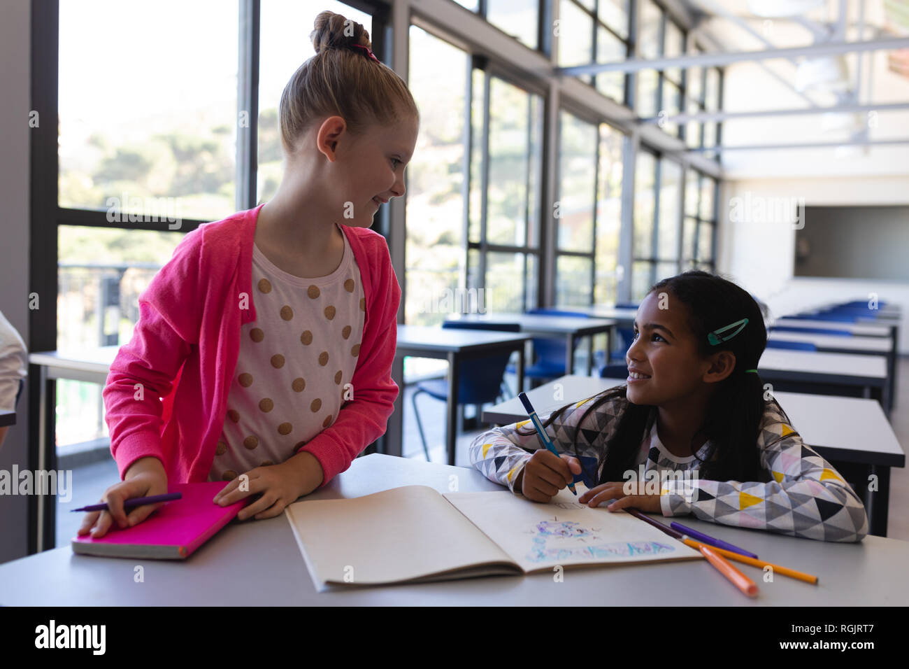 Schoolkids talking with each other at desk in classroom Stock Photo - Alamy