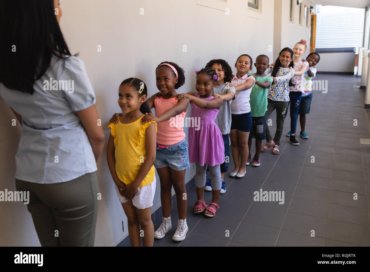 Front view of schoolkids with teacher standing in row with their hands ...