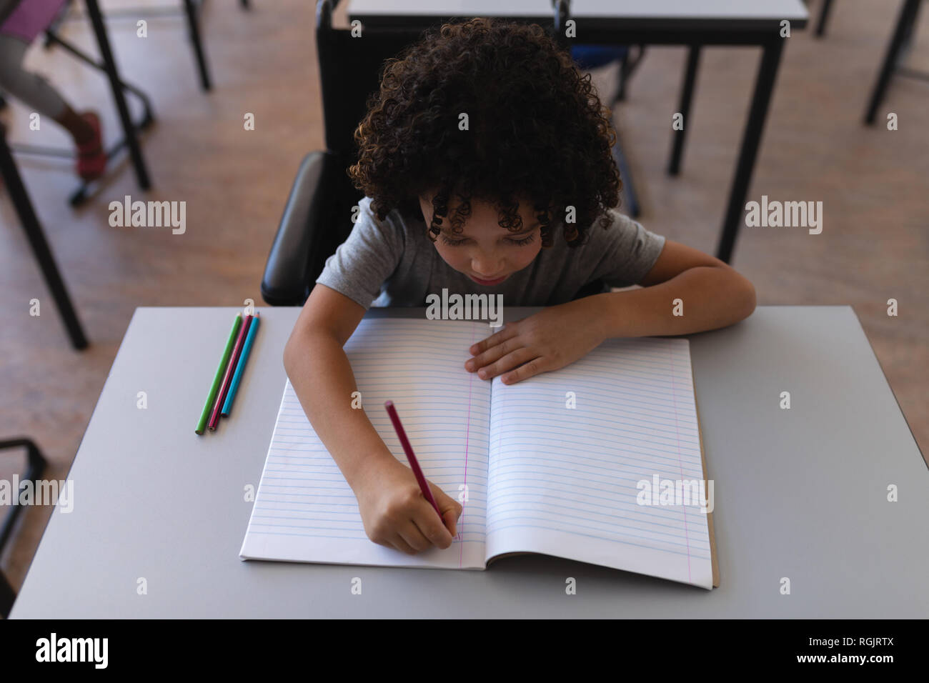Schoolboy writing on notebook at desk in classroom Stock Photo - Alamy