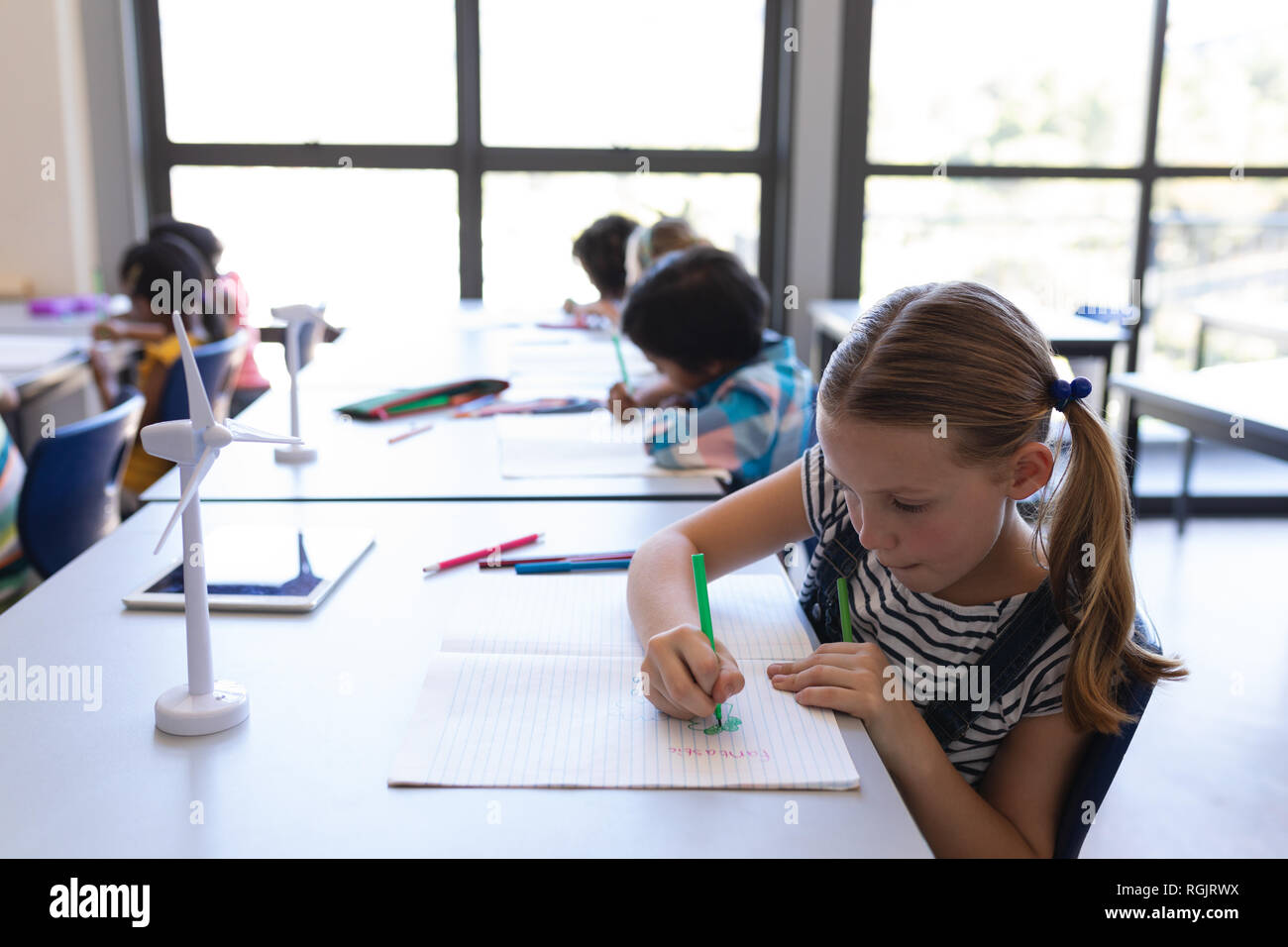 Side view of schoolgirl drawing on book at desk in classroom of ...